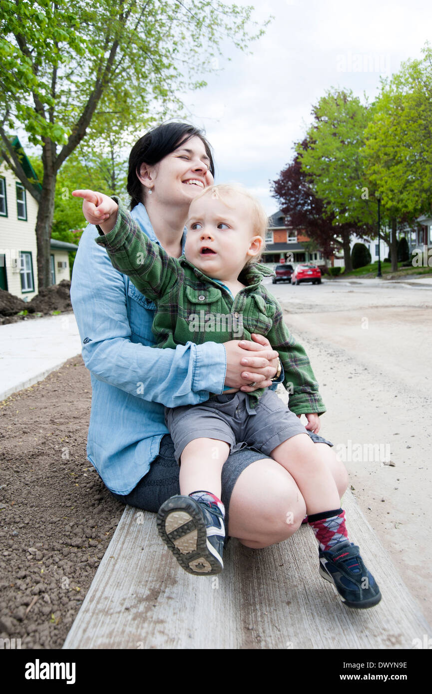Toddler sitting on mother's lap outdoors on curb near road Stock Photo ...