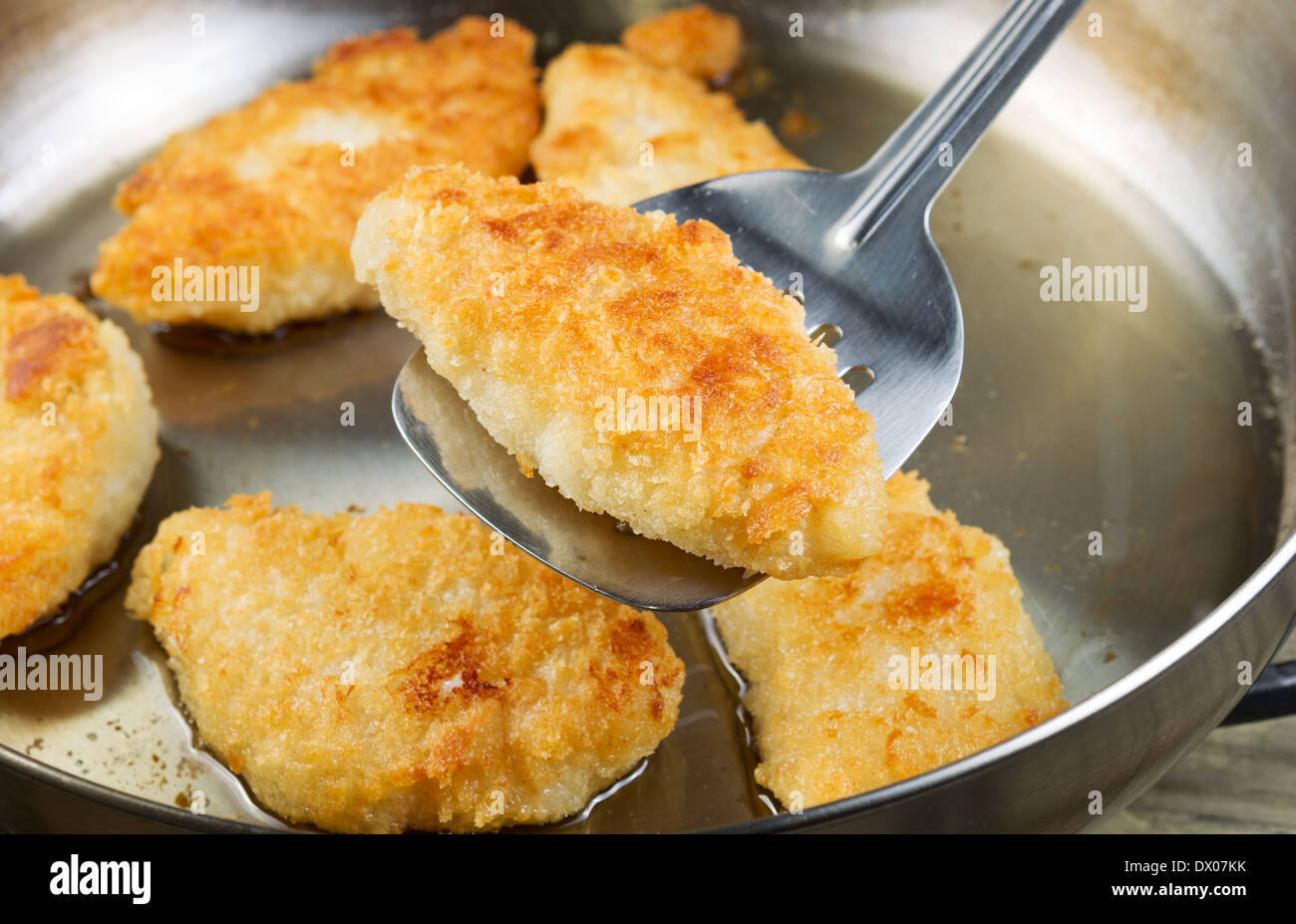 Horizontal photo of golden breaded coated fish being fried in stainless ...