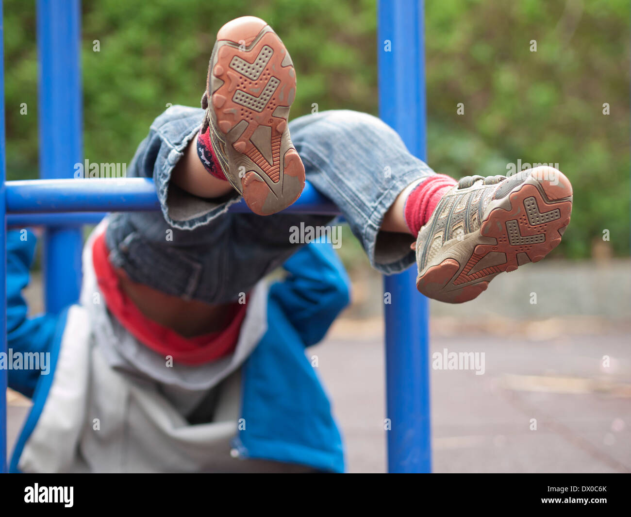 Child hanging upside down in climbing frame of a playground. Focus on ...