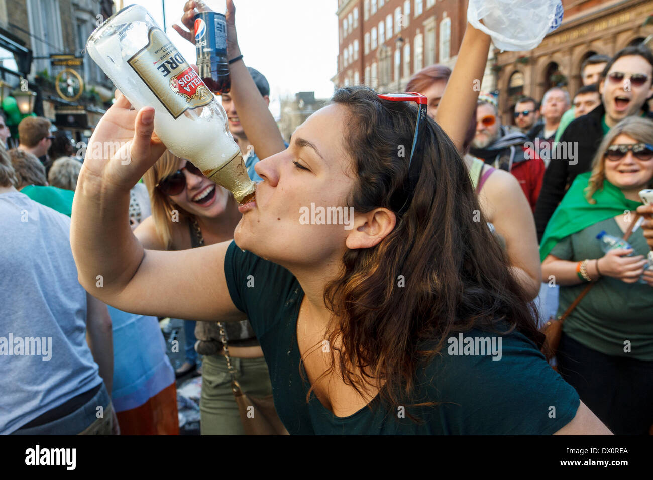 A young woman drinks cider from a bottle as she is encouraged by ...