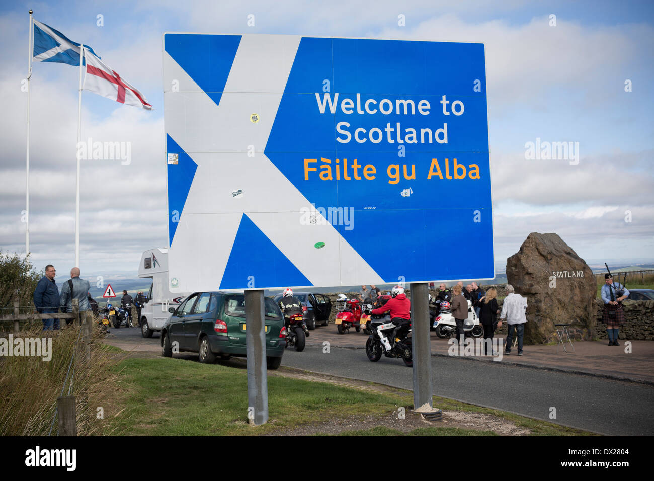 People walking by a large blue road sign marking the border between ...