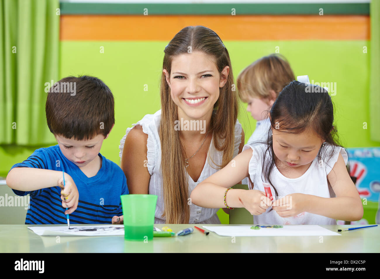 Happy child care worker with children drawing in a kindergarten Stock ...
