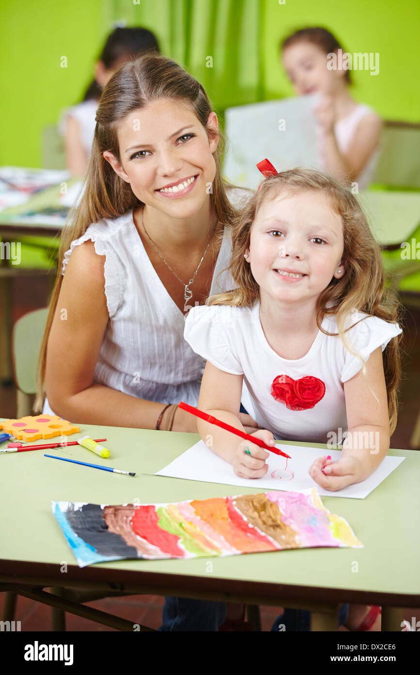 Happy child care worker helping girl painting in a kindergarten Stock ...