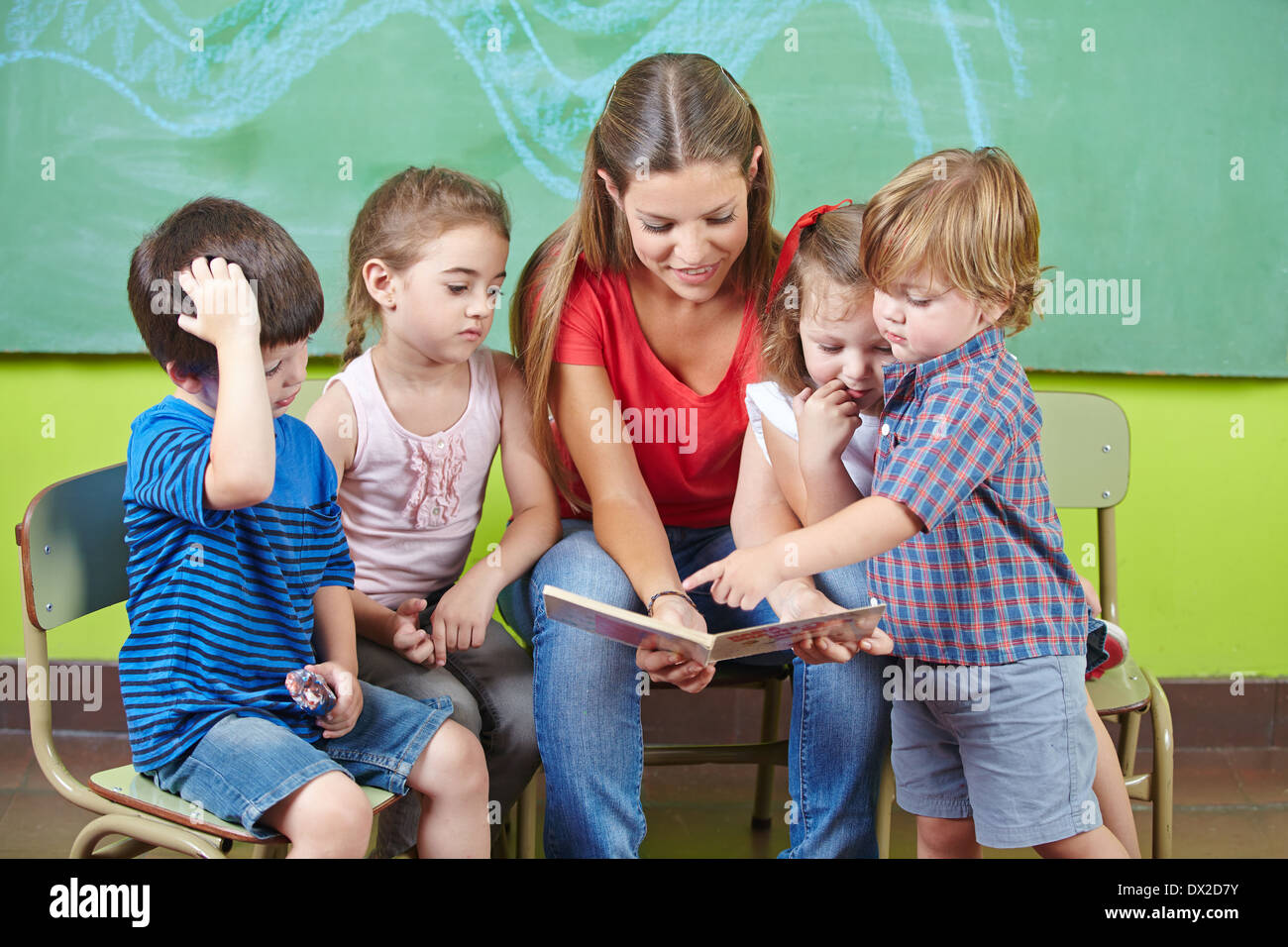 Children and nursery teacher reading book together in kindergarten ...