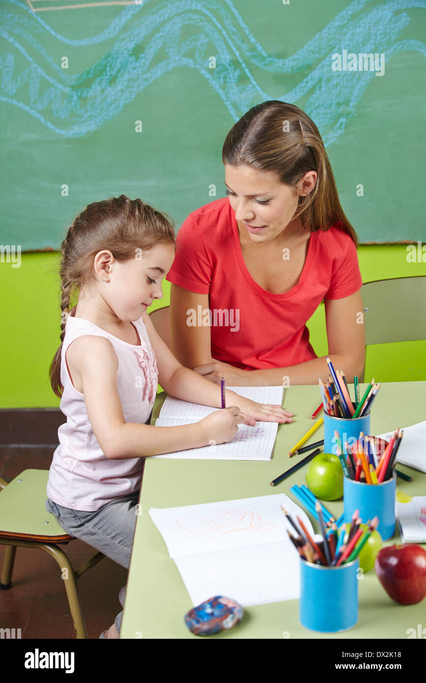 Girl learning to write in preschool class with nursery teacher Stock ...