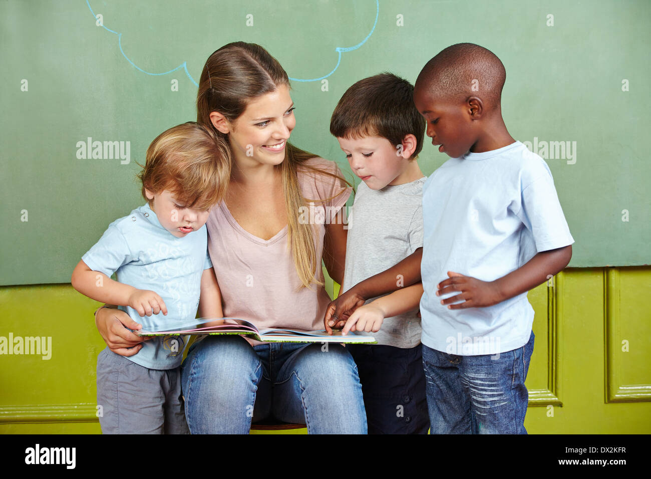 Happy child day care worker with children reading a book in ...