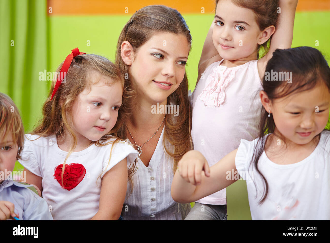 Woman as child care worker in kindergarten with a group of children ...