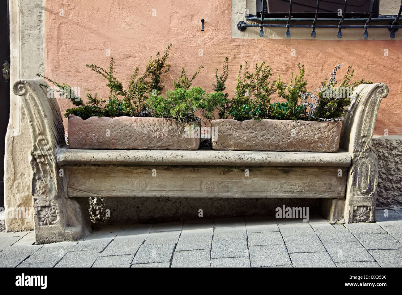 Vintage stone bench with flower beds stands against a wall in old town ...