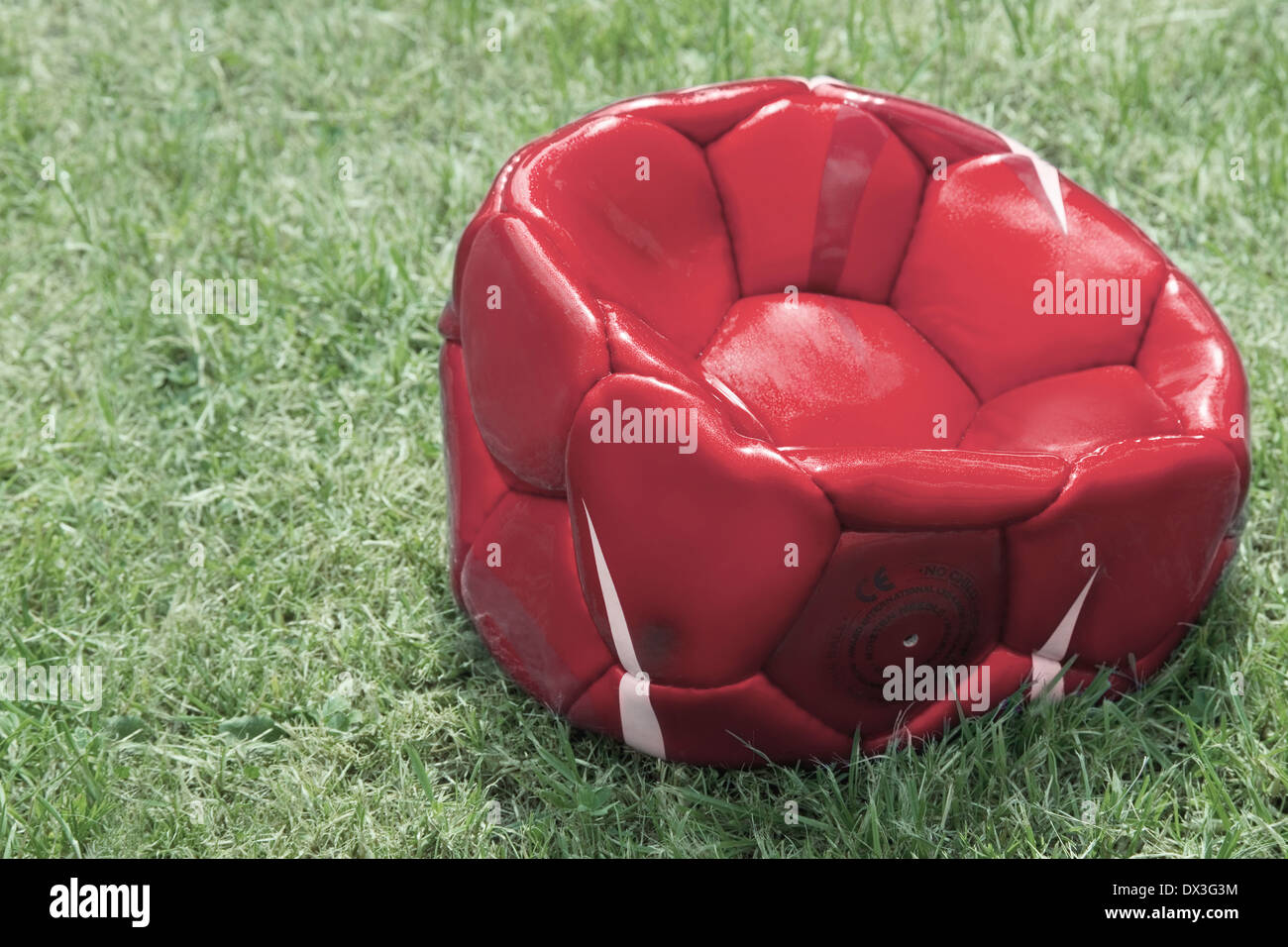 Red Punctured football on a grass pitch Stock Photo - Alamy