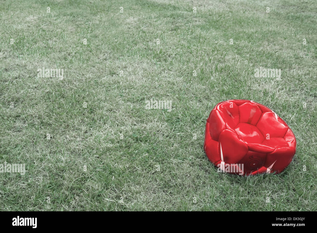 Red Punctured football on a grass pitch Stock Photo - Alamy