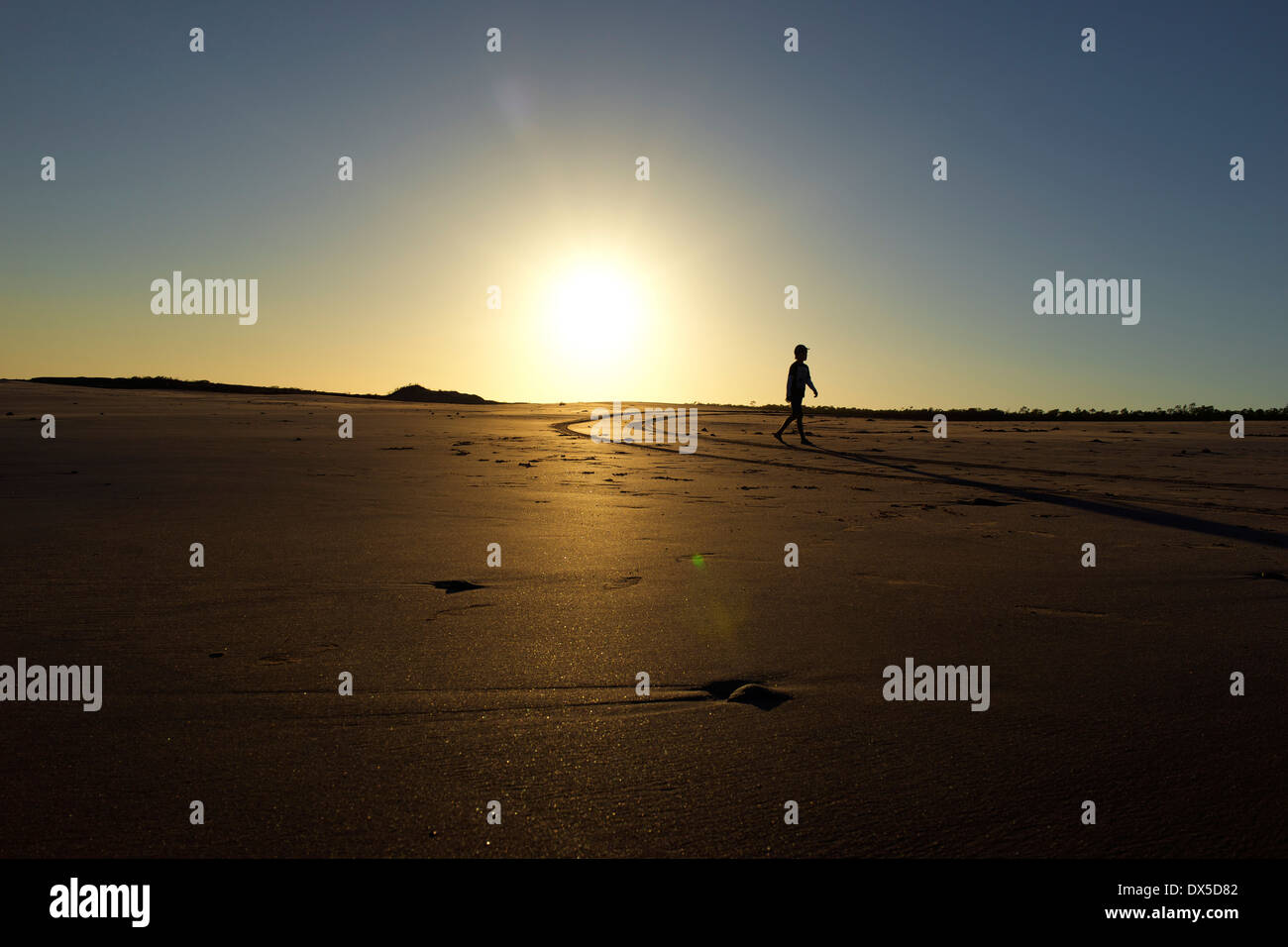 Boy walking down a remote beach at sunset Stock Photo - Alamy