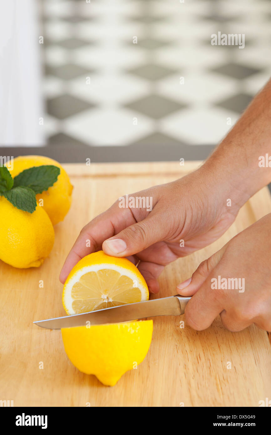 Man's hands slicing lemon into cross-section on wooden cutting board in ...