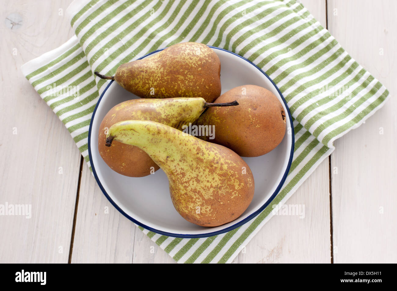 Four pears in a white bowl on a green and white striped kitchen towel ...