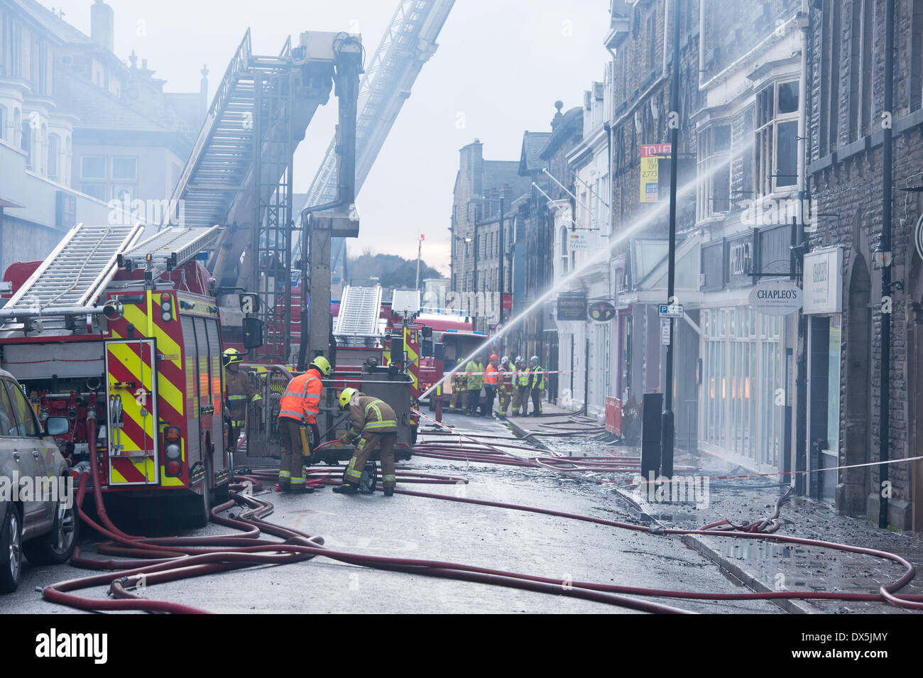 Firefighters by engines & burning building, tackle fire with water jet ...