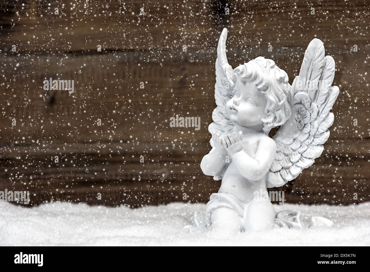 little white guardian angel in snow on wooden background. vintage style ...