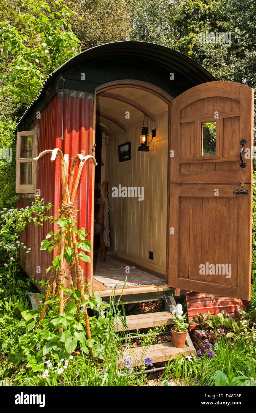 An old gypsy caravan seen surrounded by plants and shrubbery with door ...