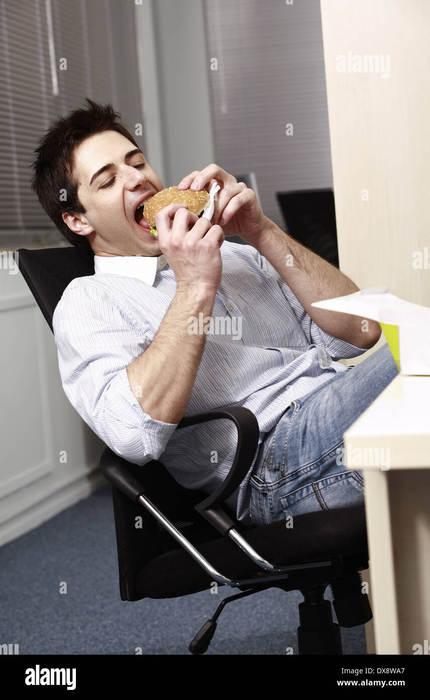 Office worker eating hamburger at desk Stock Photo - Alamy