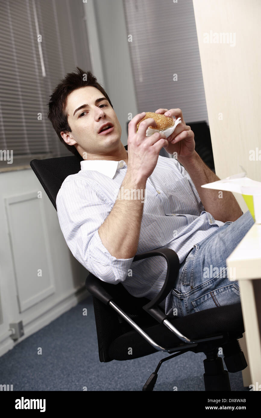 Office worker eating hamburger at desk Stock Photo - Alamy