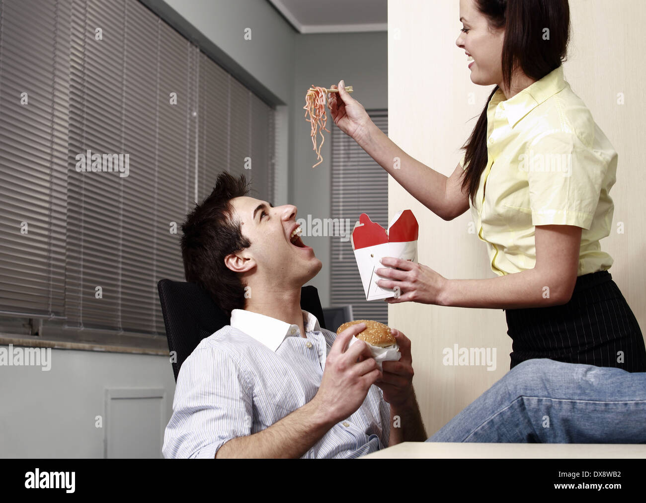 Office worker feeding her colleague at desk Stock Photo - Alamy