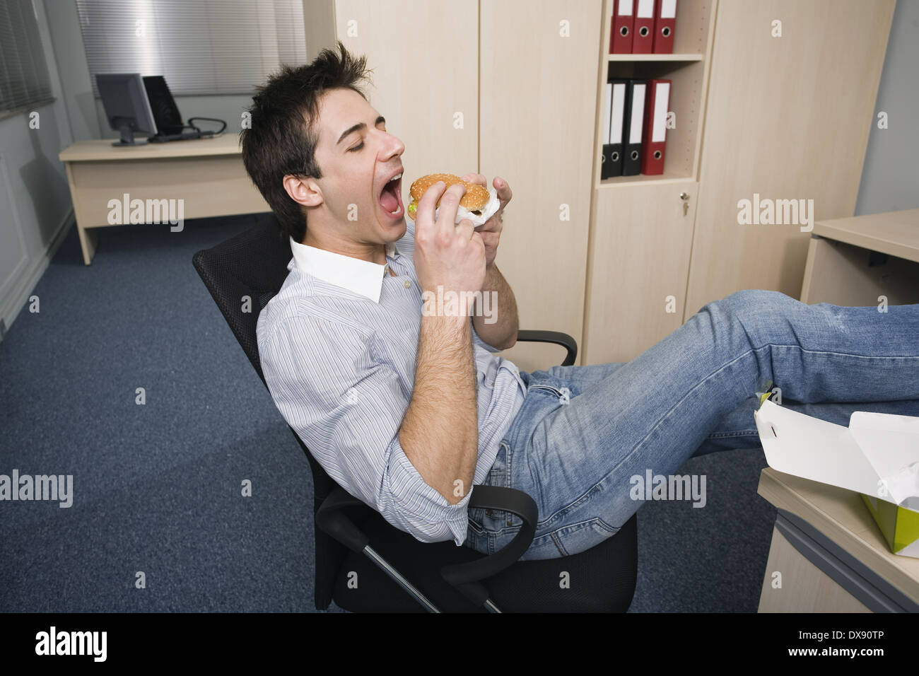 Office worker taking a bite of a hamburger at desk Stock Photo - Alamy