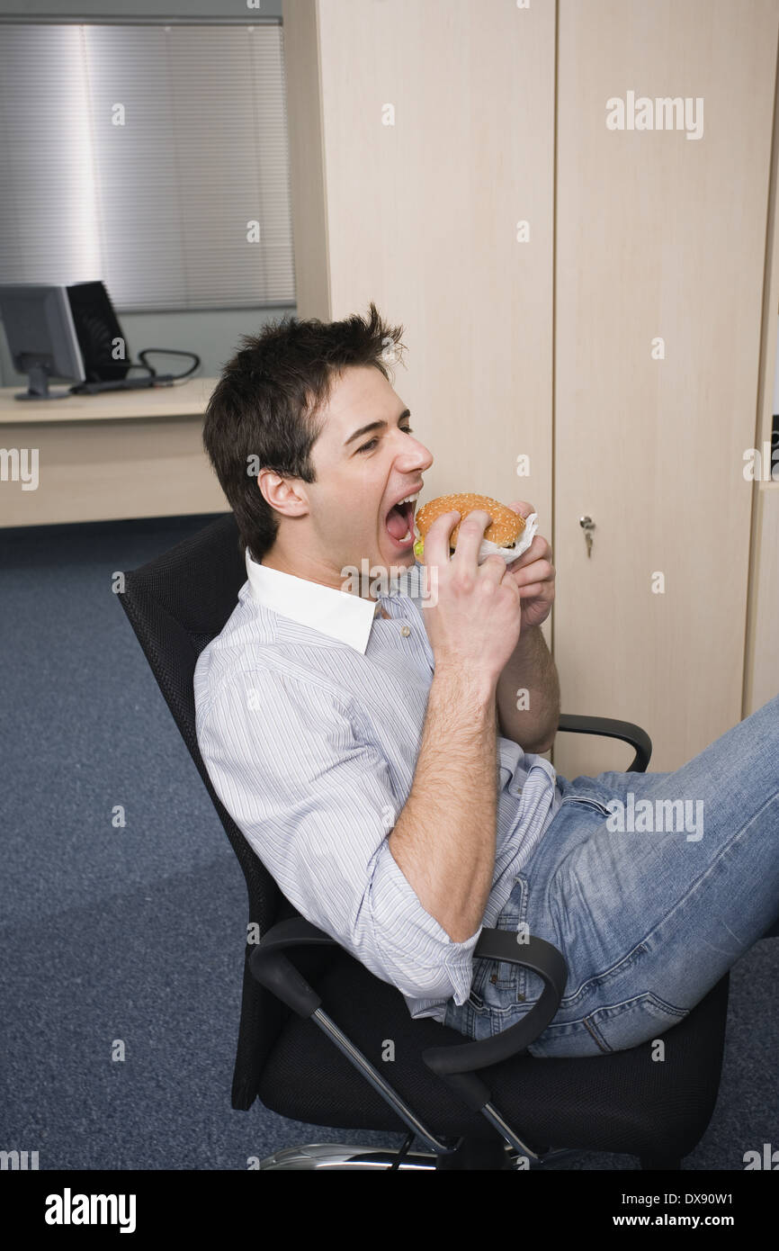 Office worker taking a bite of a hamburger at desk Stock Photo - Alamy