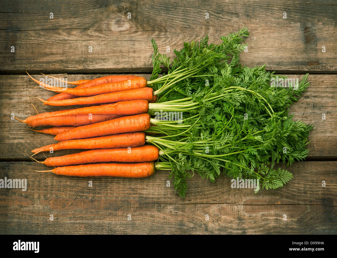 Roots of fresh carrots with green leaves over wooden background ...