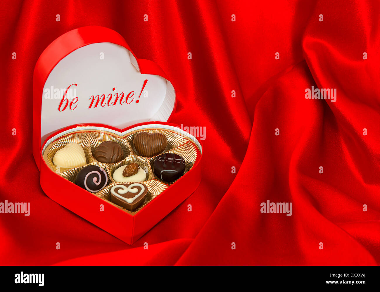 chocolate pralines in golden heart shape box over red silk background ...