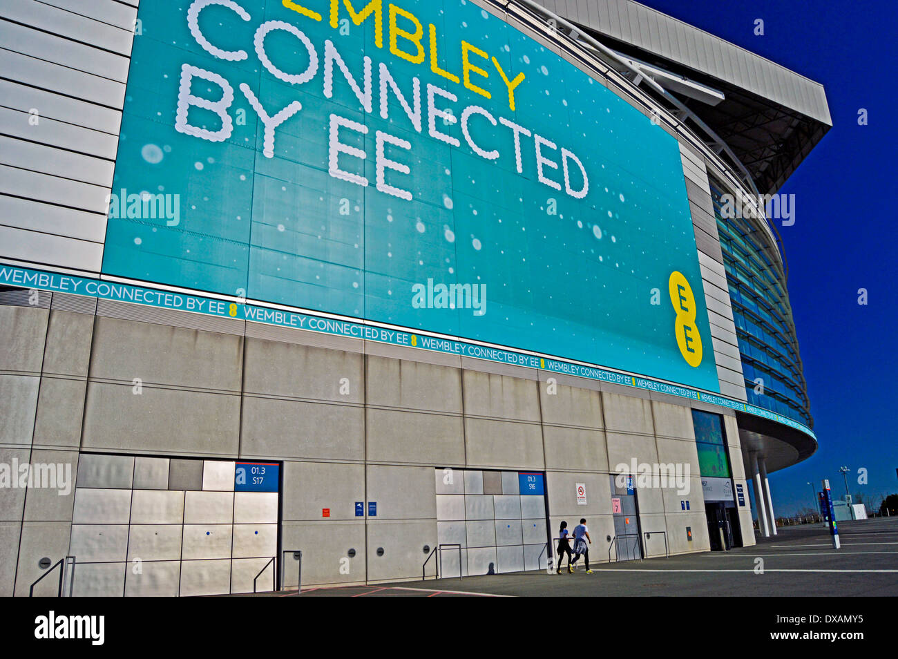 Couple jogging on Wembley Stadium concourse showing EE advertisement ...