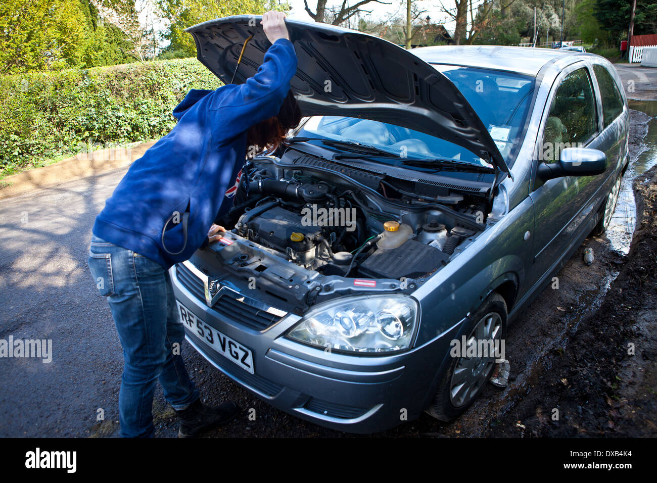 Woman looking under bonnet of broken down car Stock Photo - Alamy