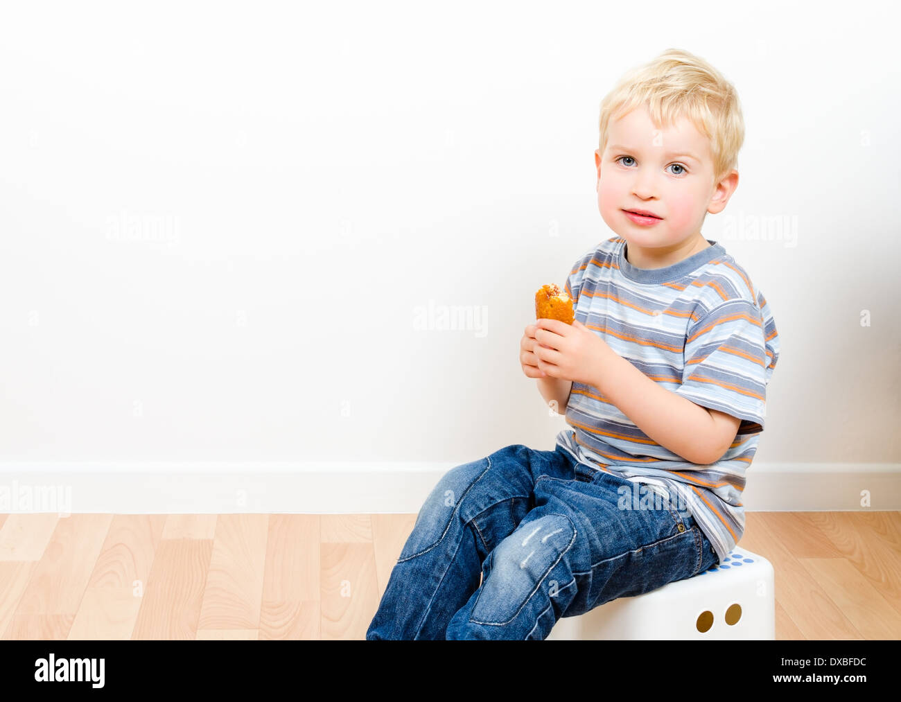 Cute little boy eating delicious cookie sitting on stool at home Stock ...
