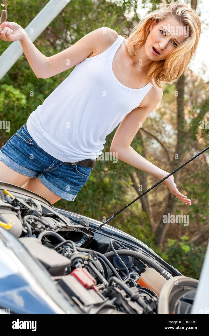 Attractive young blond woman inspecting her car engine after a ...