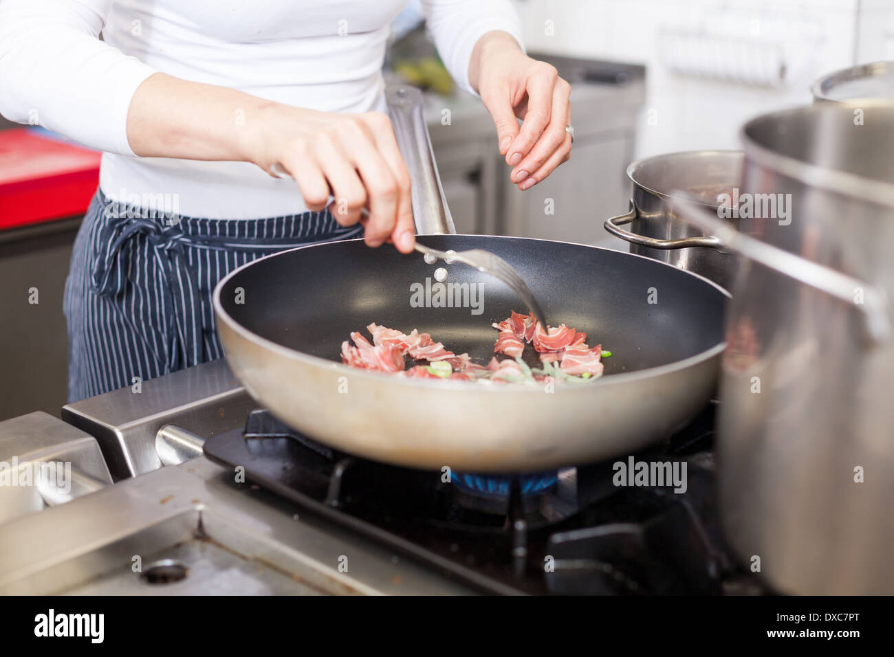 Chef or cook braising meat in a non-stick frying pan over a gas hob as ...