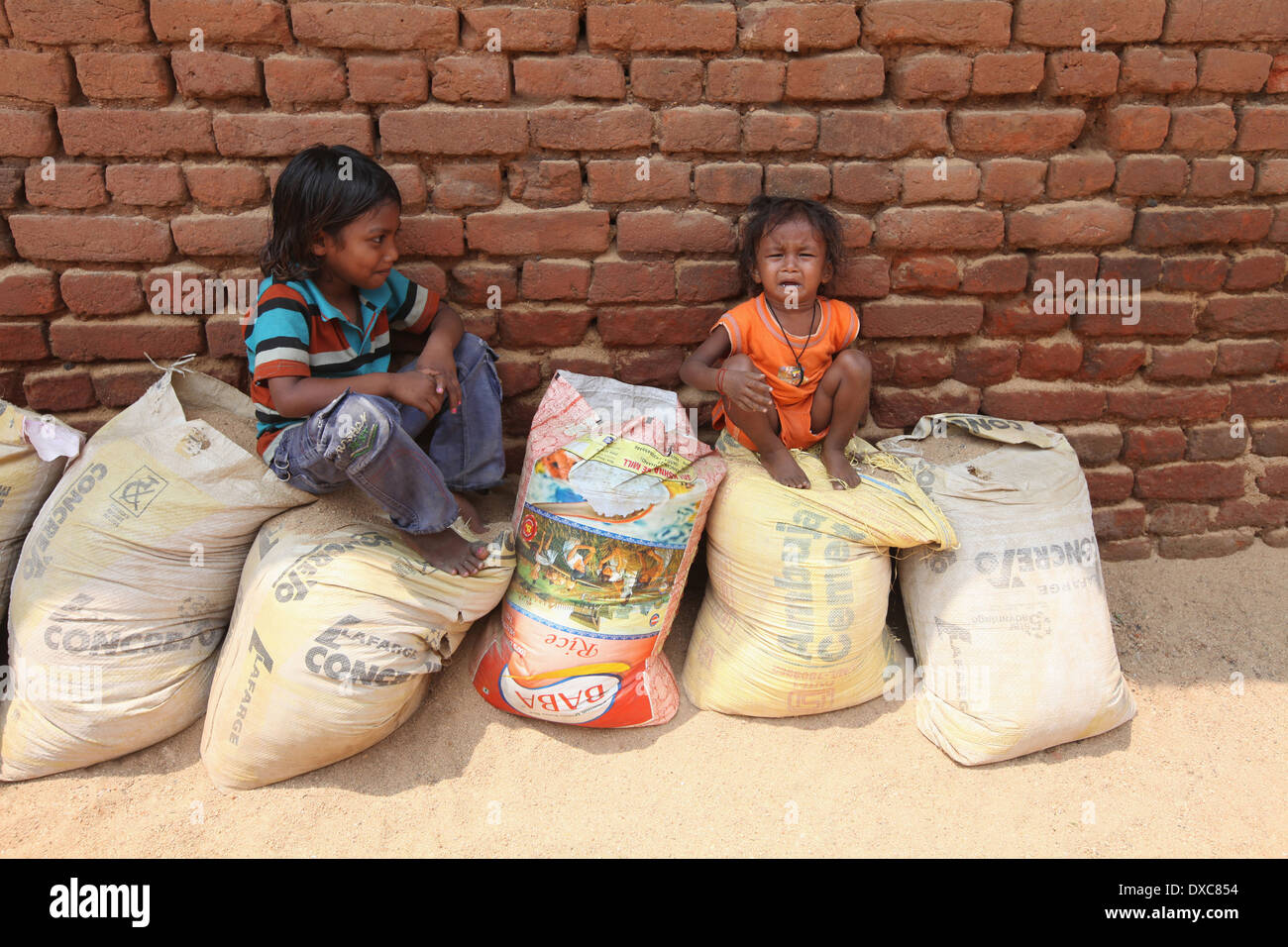 Child crying and sibling watching amusedly. Sitting on cement bags ...