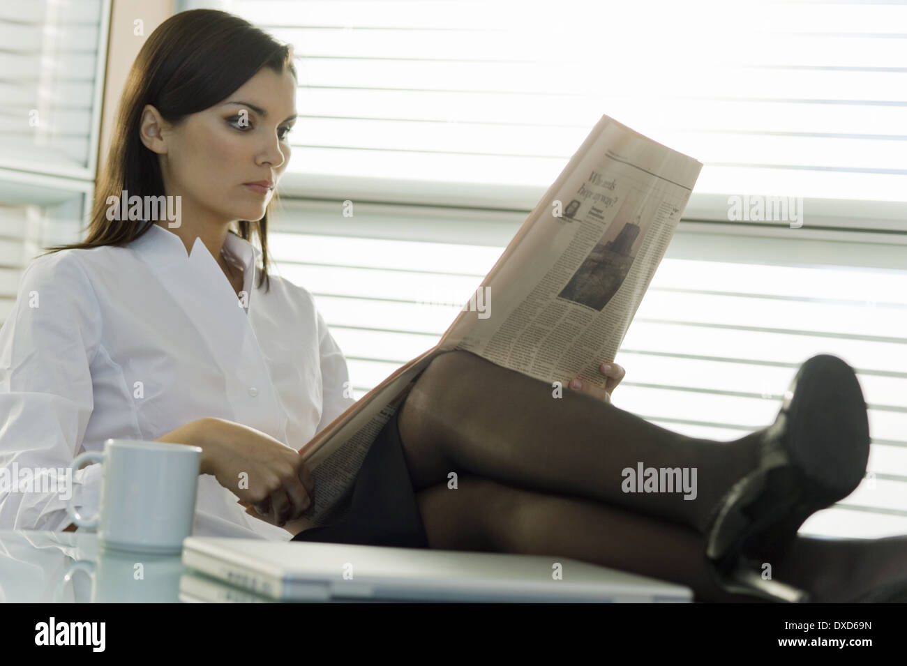 Professional woman reading newspaper with legs up on desk Stock Photo ...