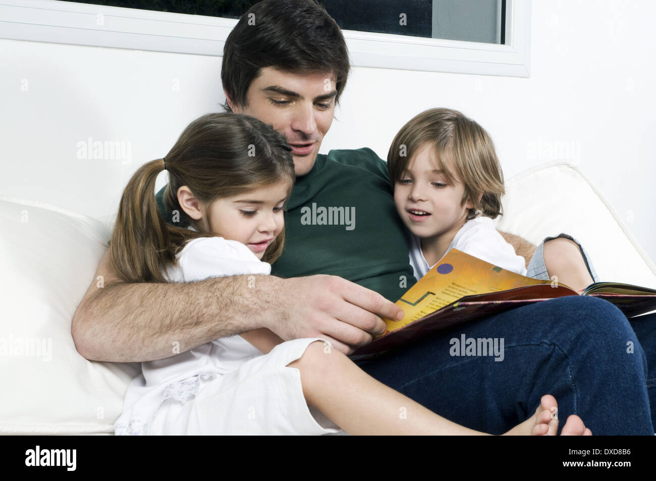 Young man on couch with children reading Stock Photo - Alamy