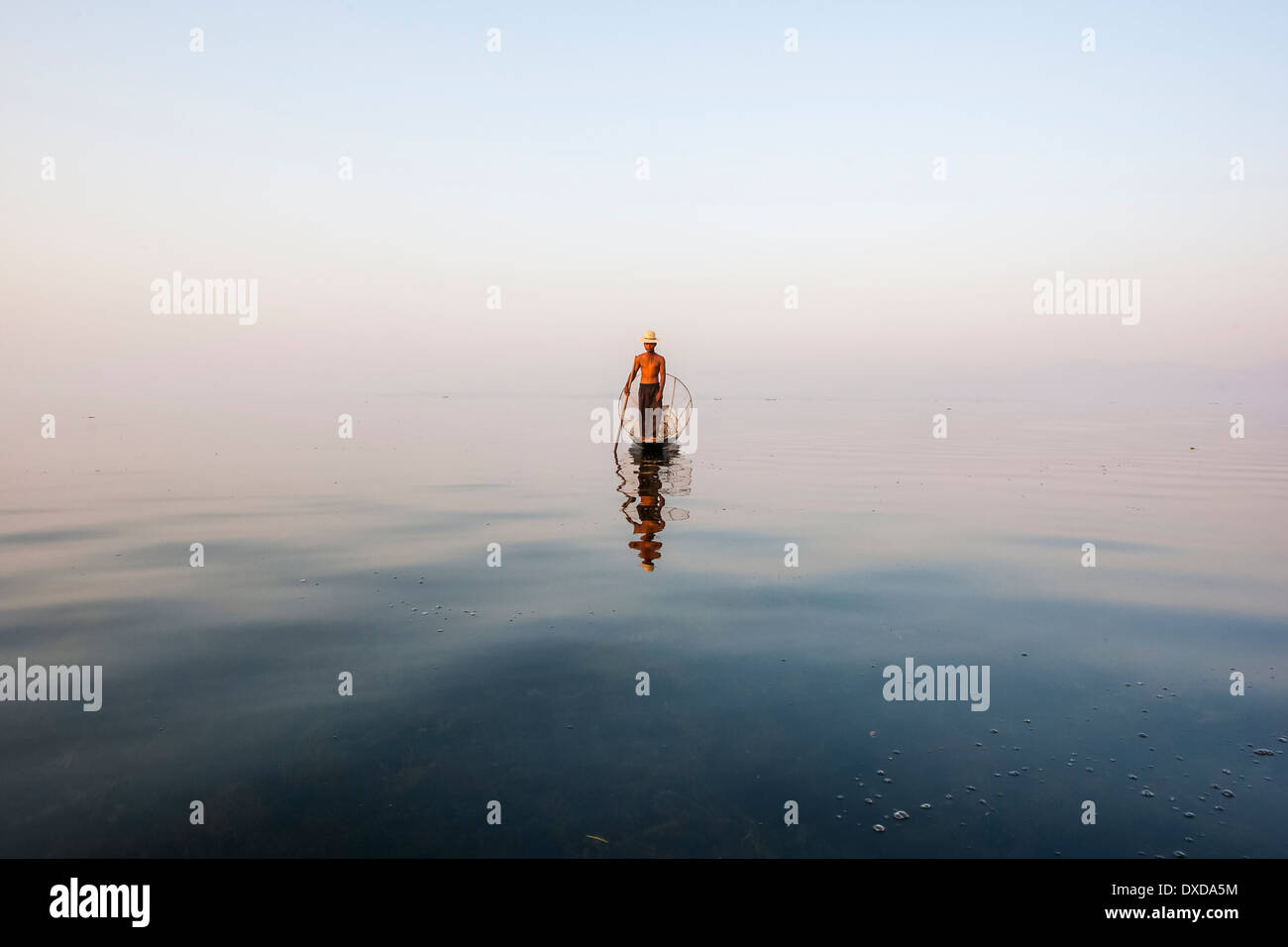 A leg rowing fisherman maneuvers his canoe and net over fish before ...