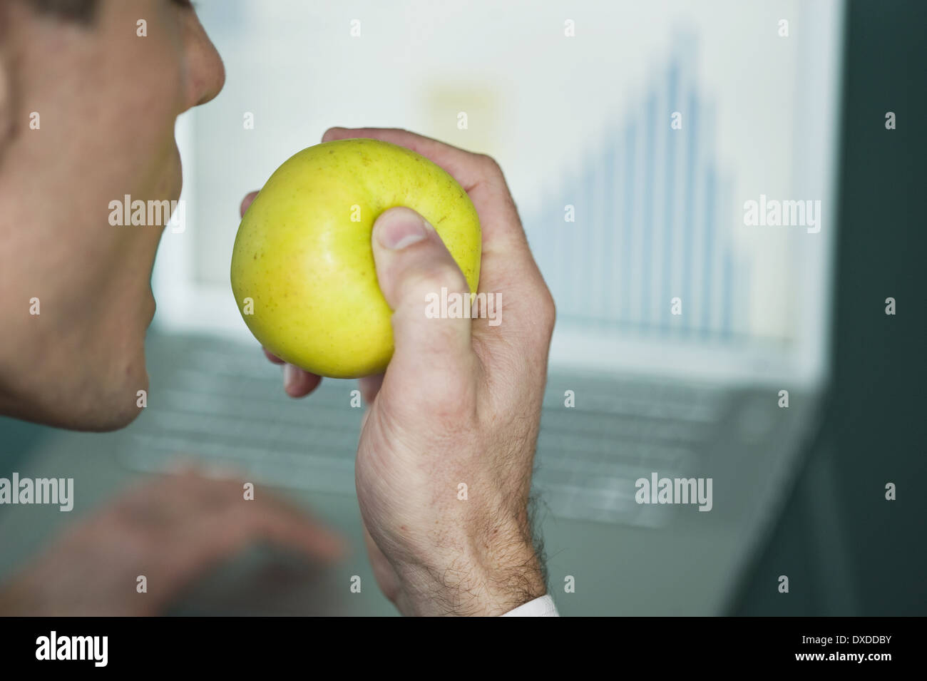 Businessman eating apple at laptop with bar chart Stock Photo - Alamy