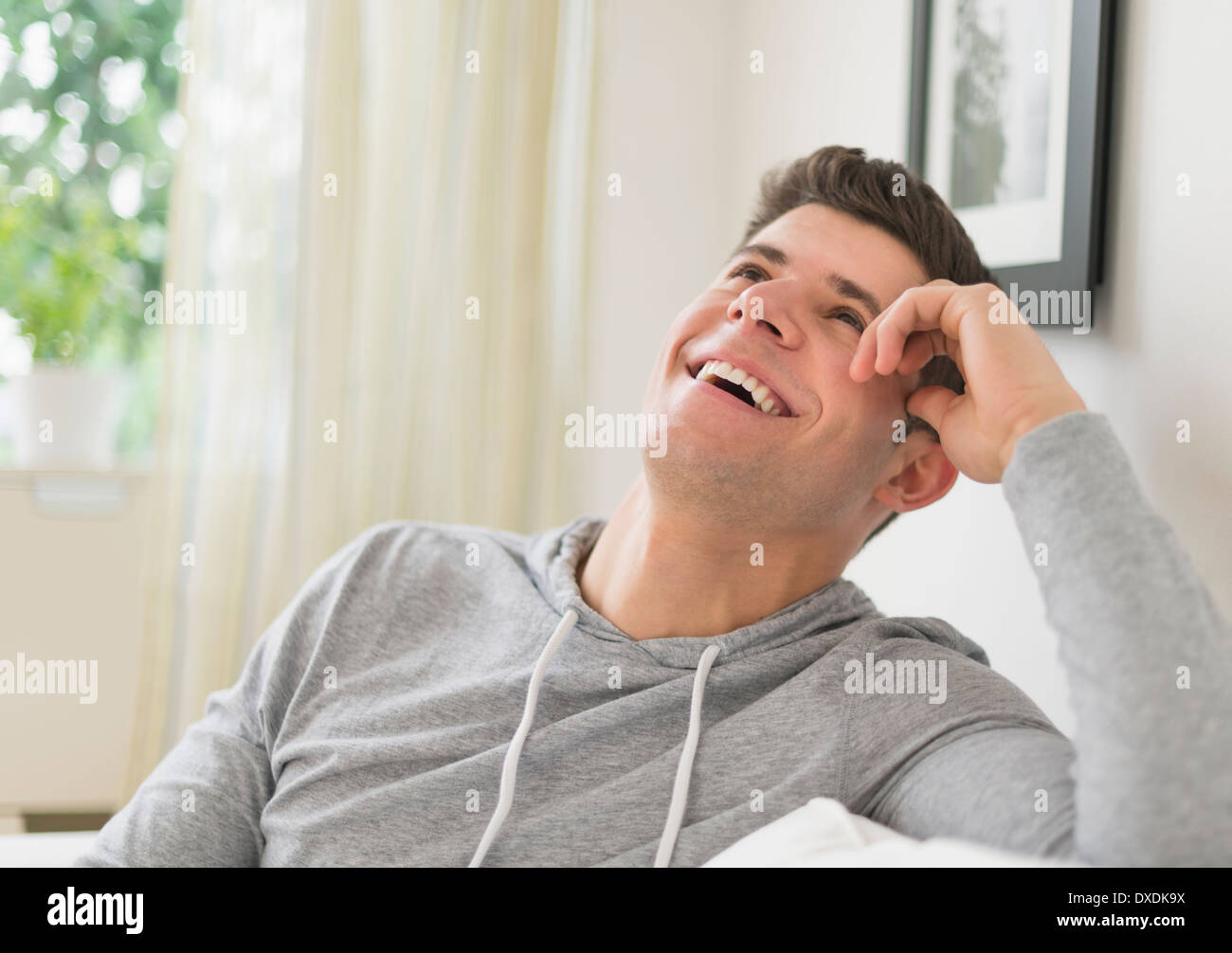 Young man sitting on sofa and smiling Stock Photo - Alamy