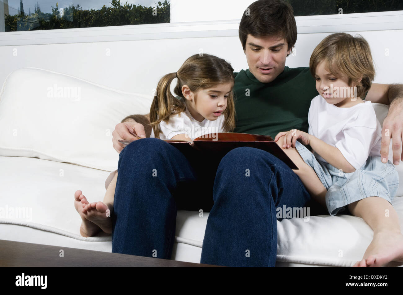 Young man on couch with children reading Stock Photo - Alamy