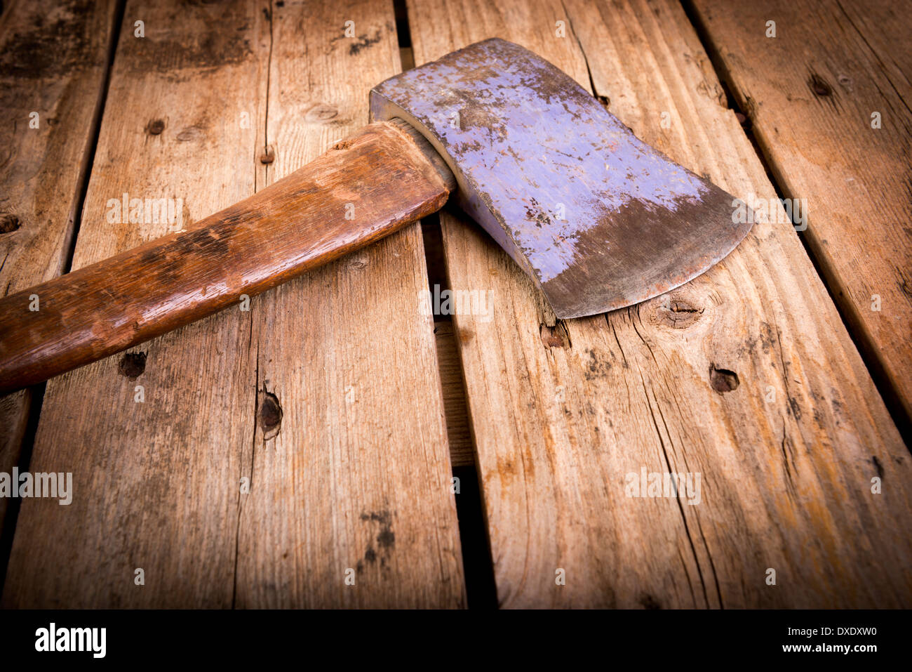 An old axe with a wooden handle and wear marks sits on a rough timber ...
