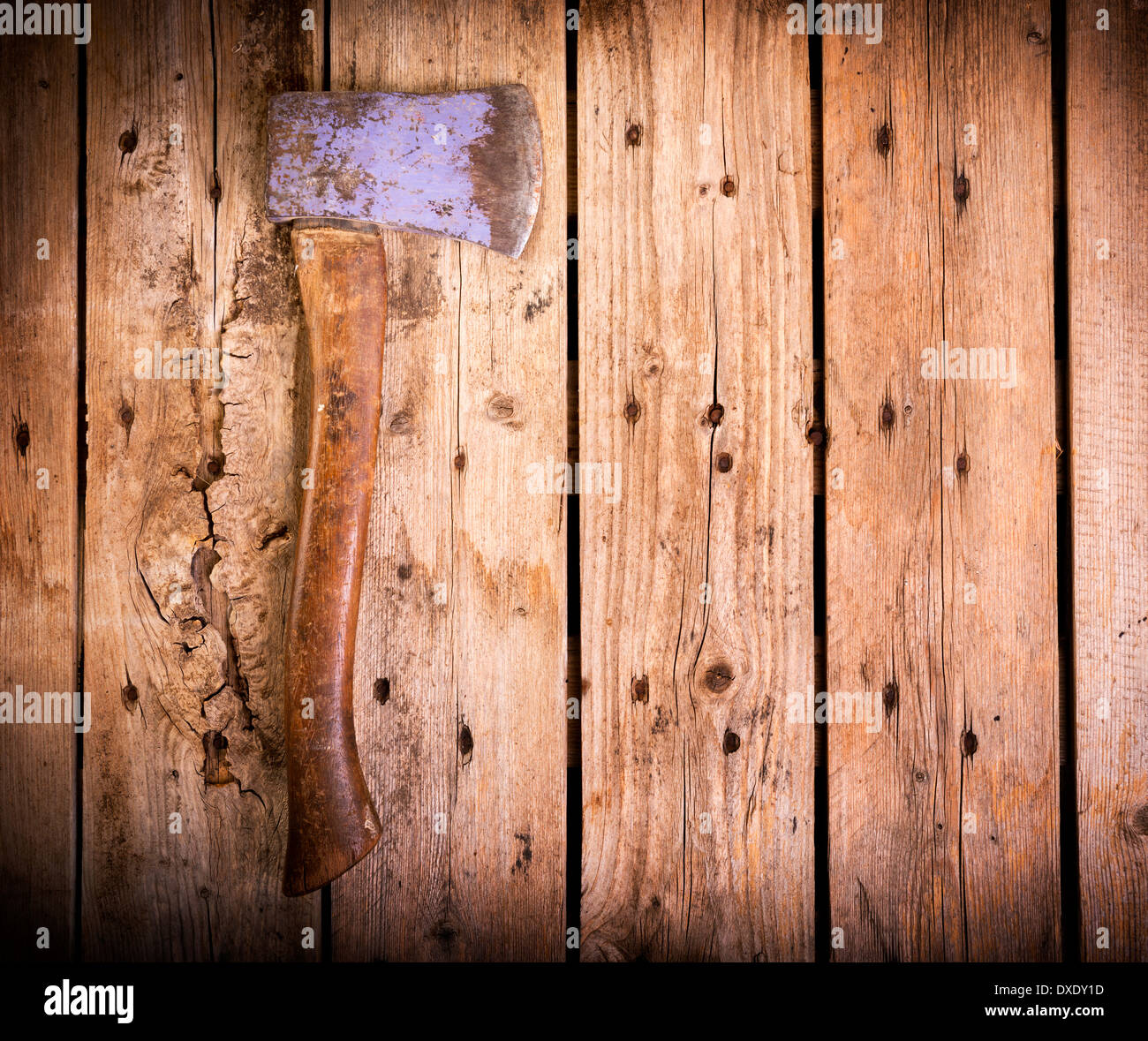 An old axe with a wooden handle and wear marks sits on a rough timber ...