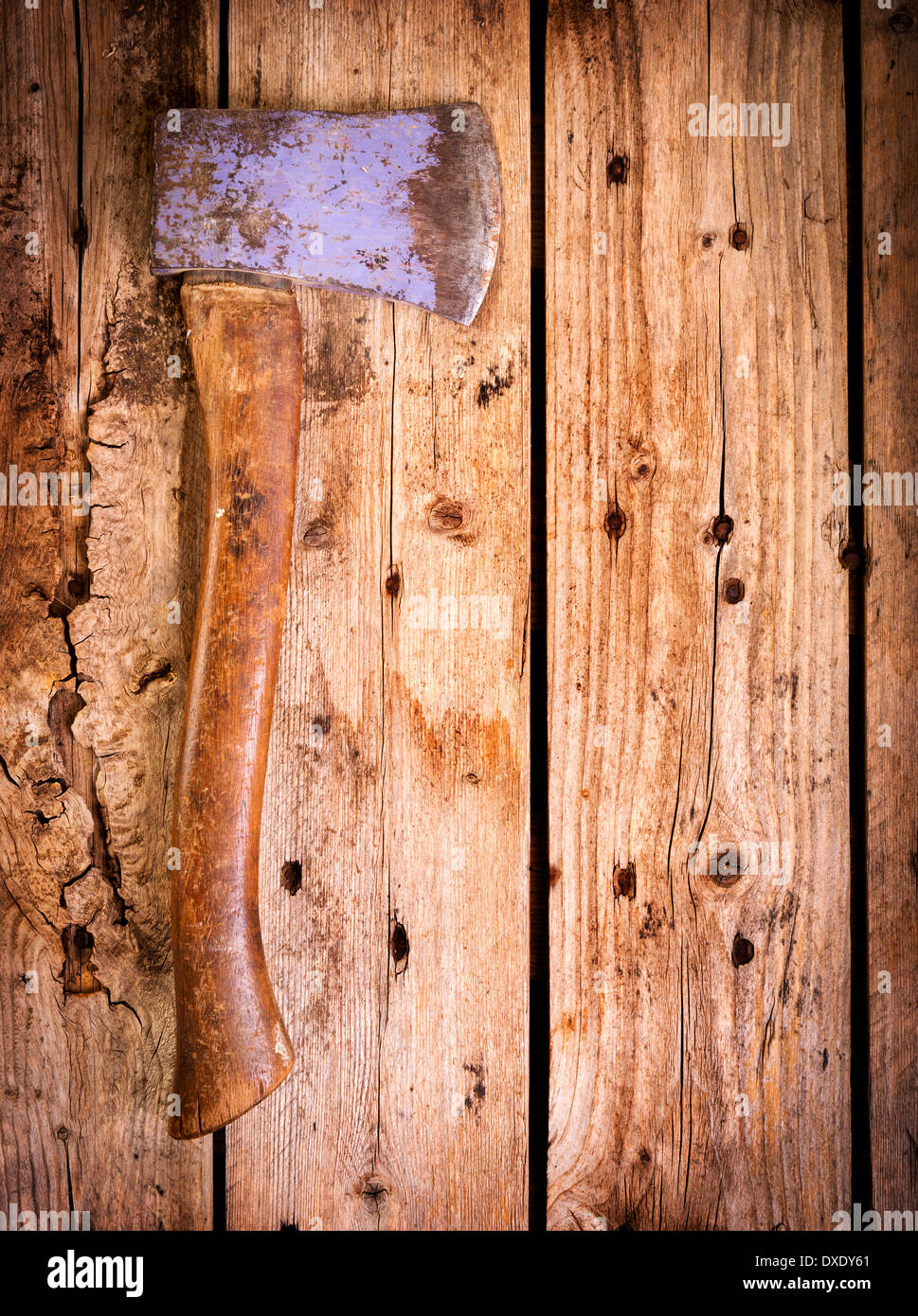 An old axe with a wooden handle and wear marks sits on a rough timber ...