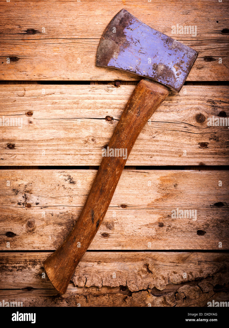 An old axe with a wooden handle and wear marks sits on a rough timber ...