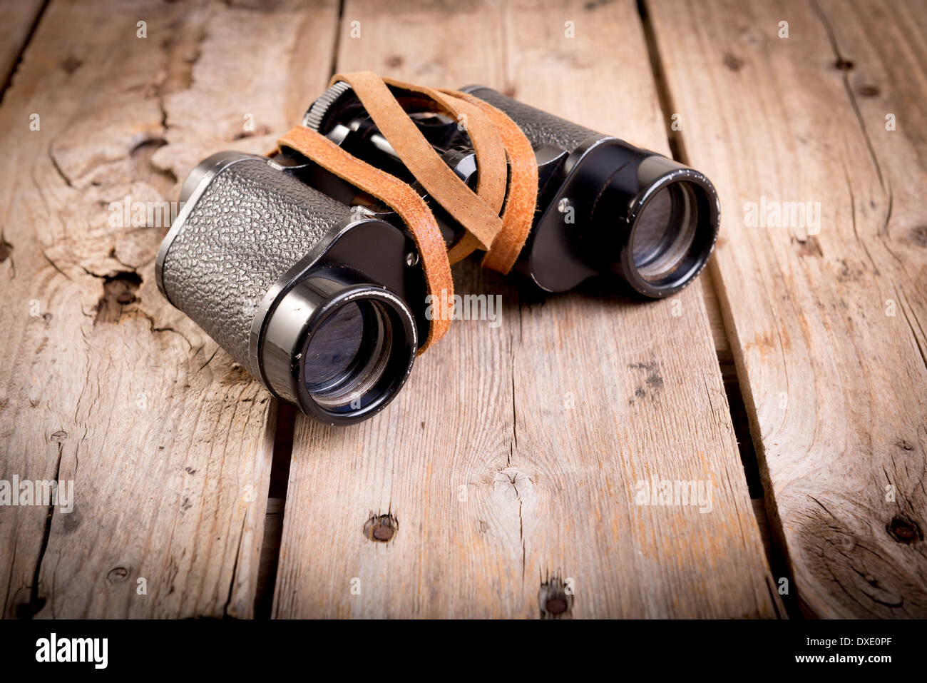 Pair of old binoculars with vintage leather strap on a rough wooden ...