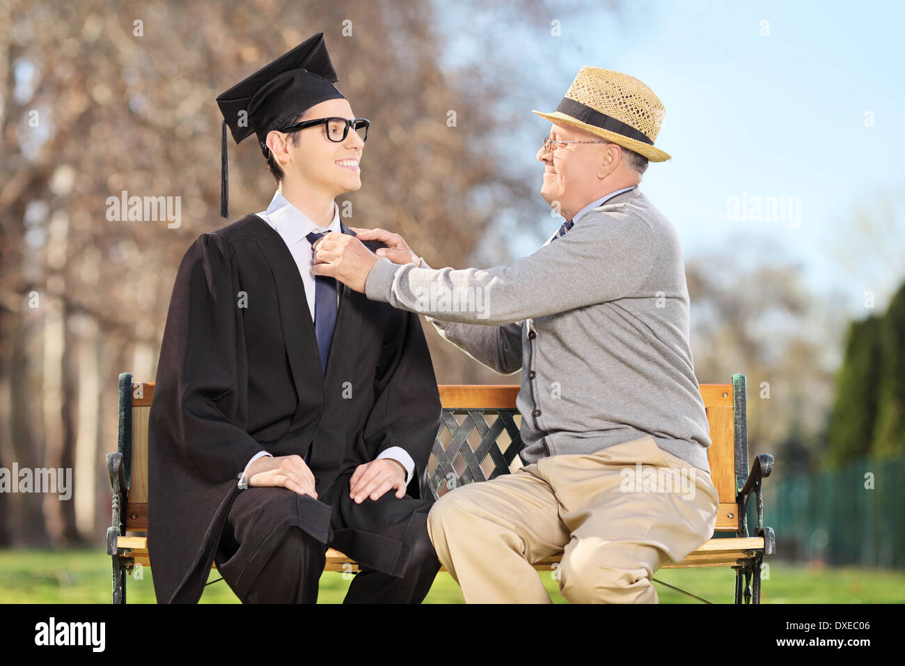 Father preparing his son for graduation seated on wooden bench in park ...