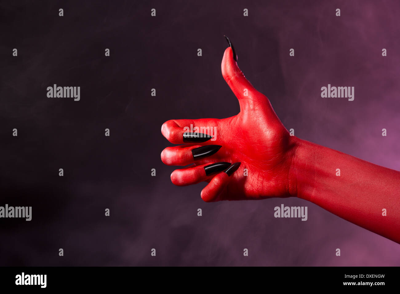 Red devil hand with black nails showing thumbs up, studio shot on smoky ...