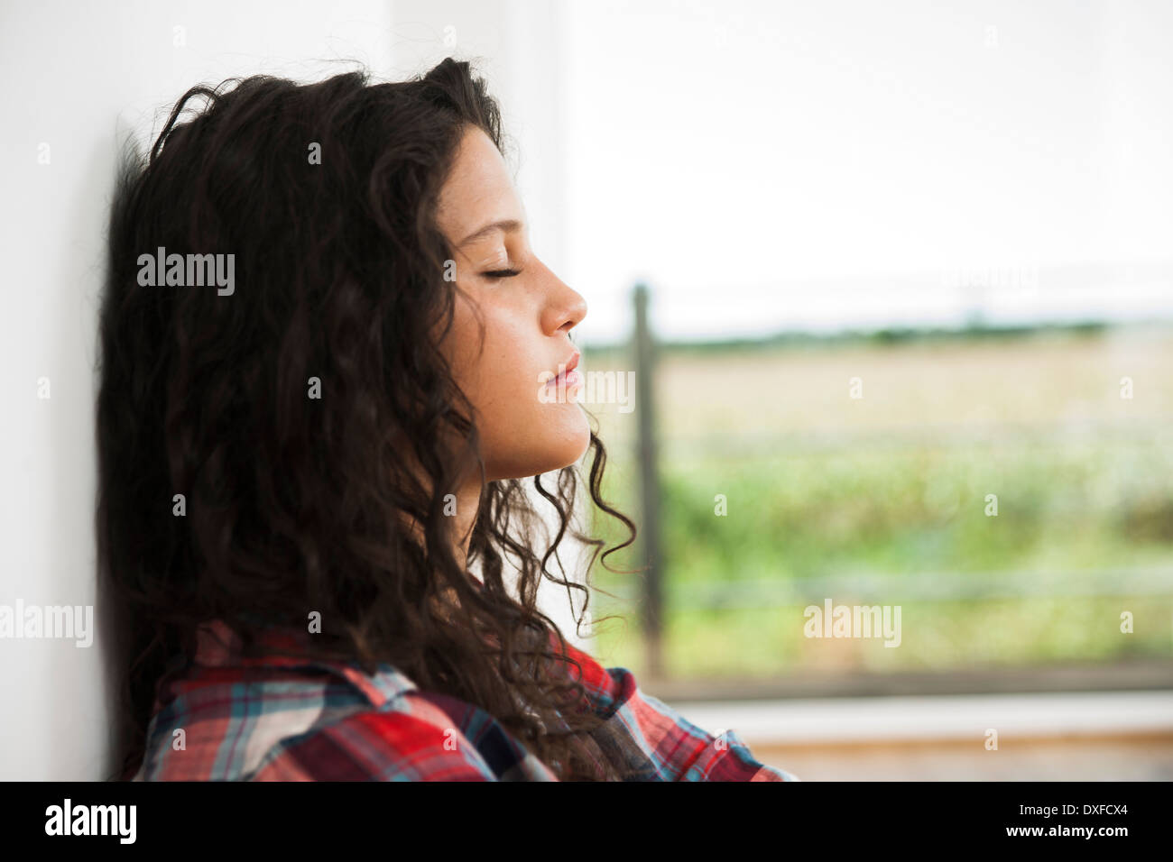 Portrait of teenage girl with eyes closed, sitting next to window ...