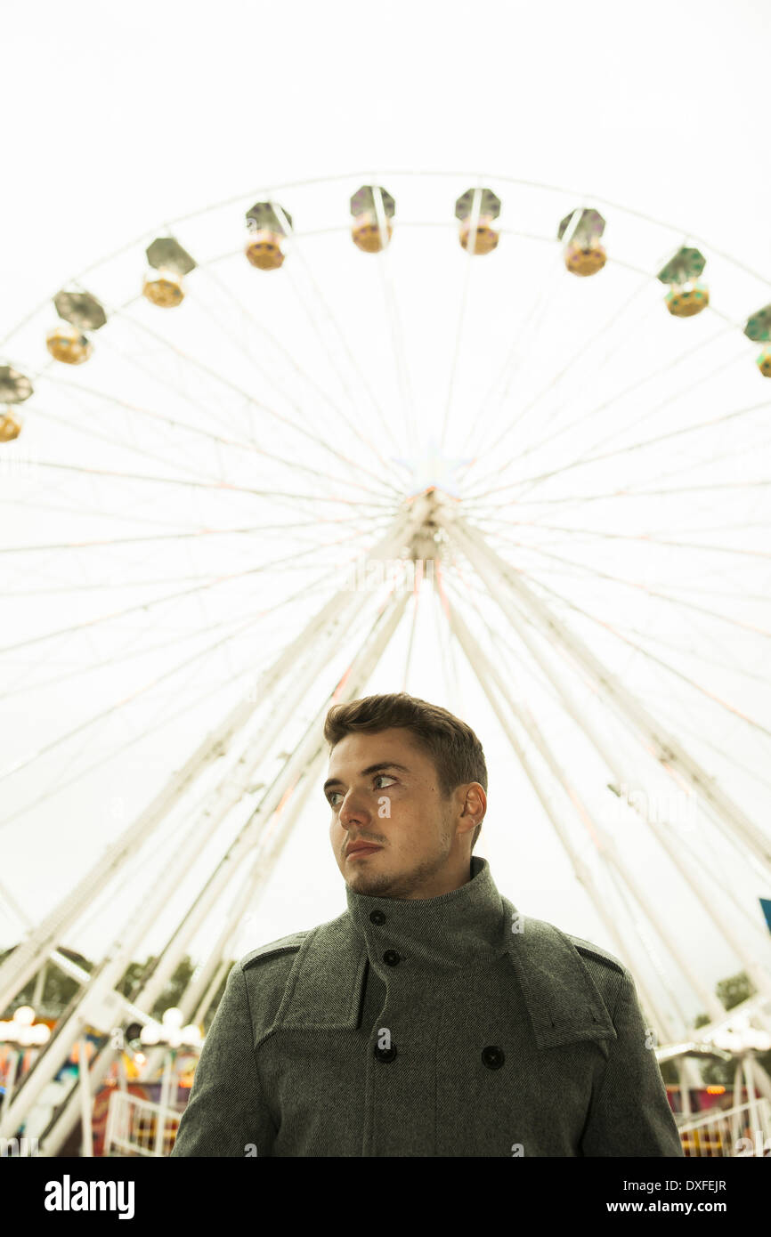 Portrait of young man standing in front of ferris wheel at amusement ...