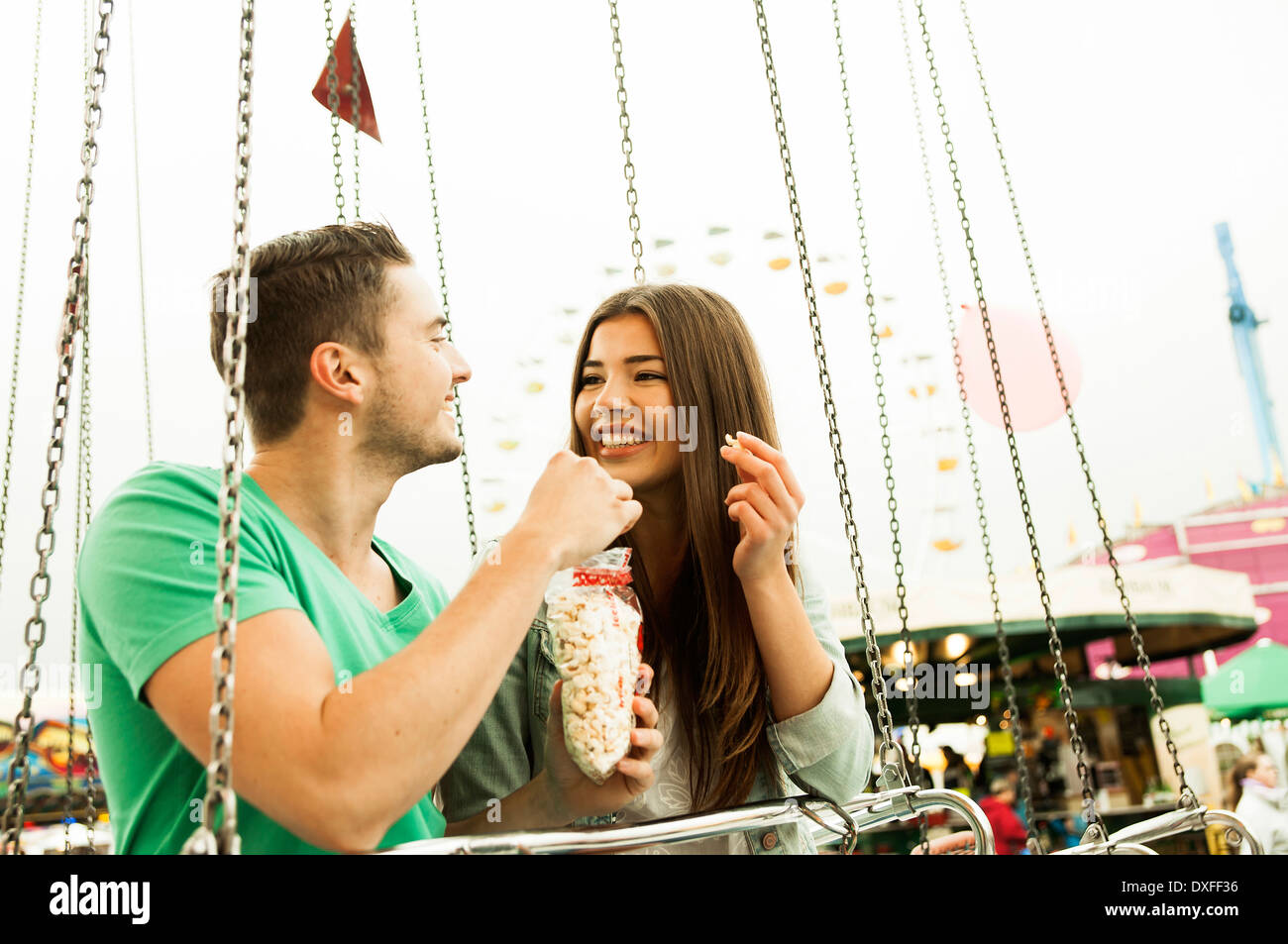 Young couple sitting on amusement park ride eating popcorn, Germany ...