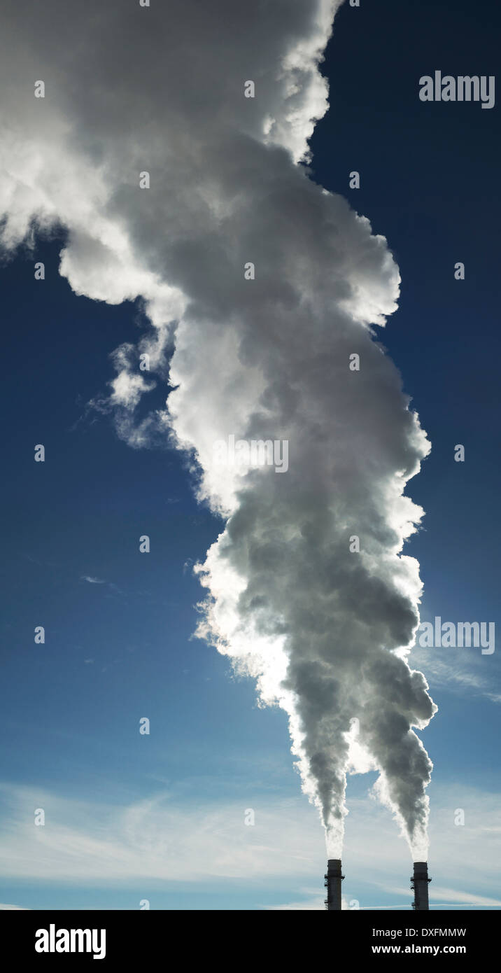 Close-up of industrial smoke stacks with steam billowing into blue sky ...